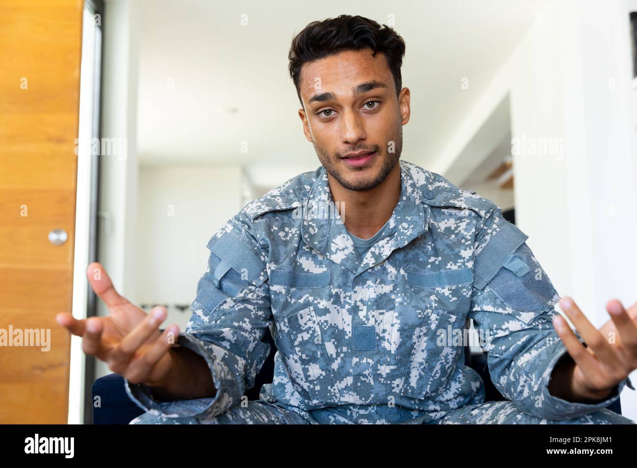 Happy biracial male soldier wearing uniform, sitting in armchair making ...