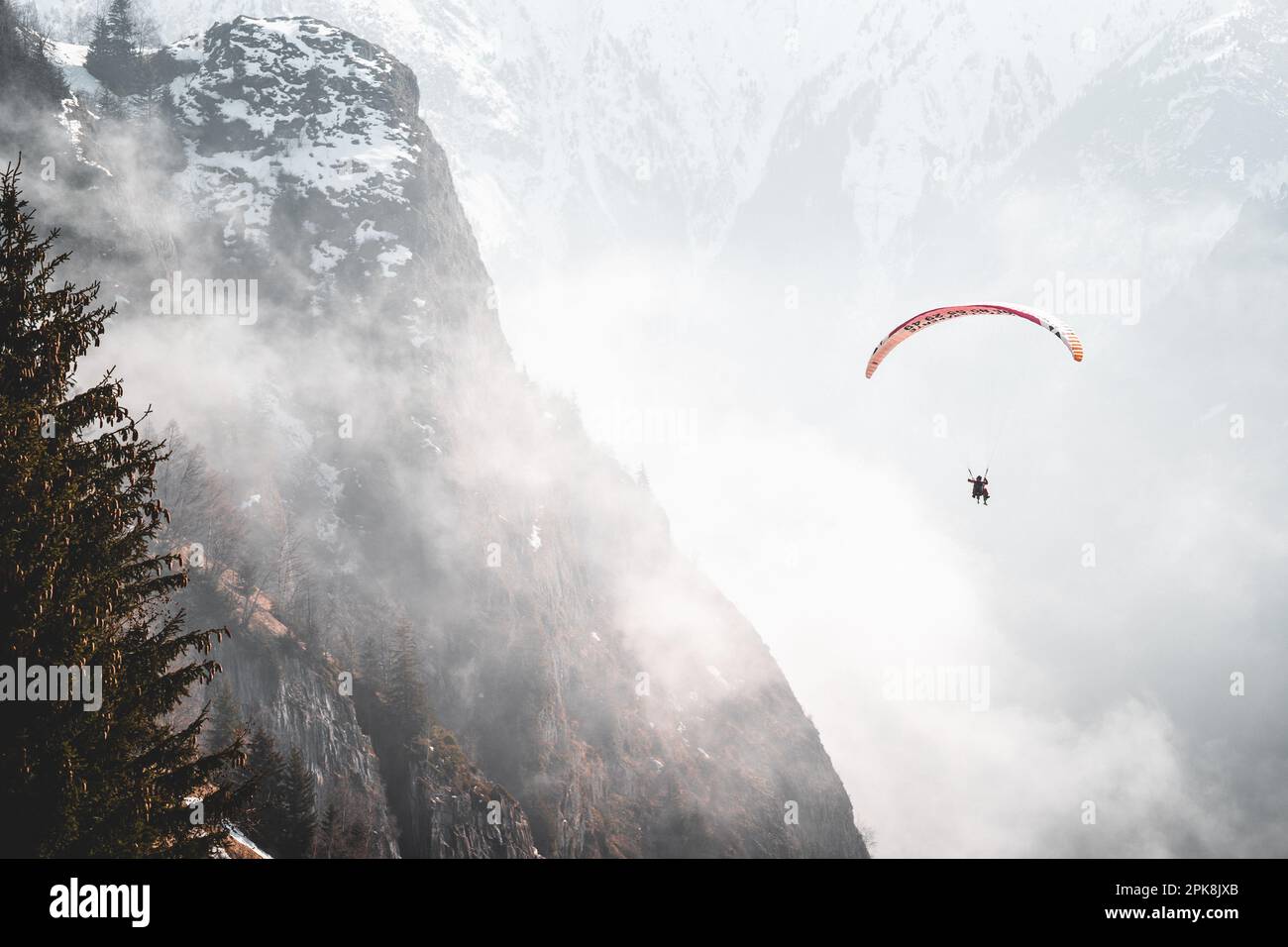 A person paragliding through the air above majestic snow-capped mountain peaks Stock Photo - Alamy