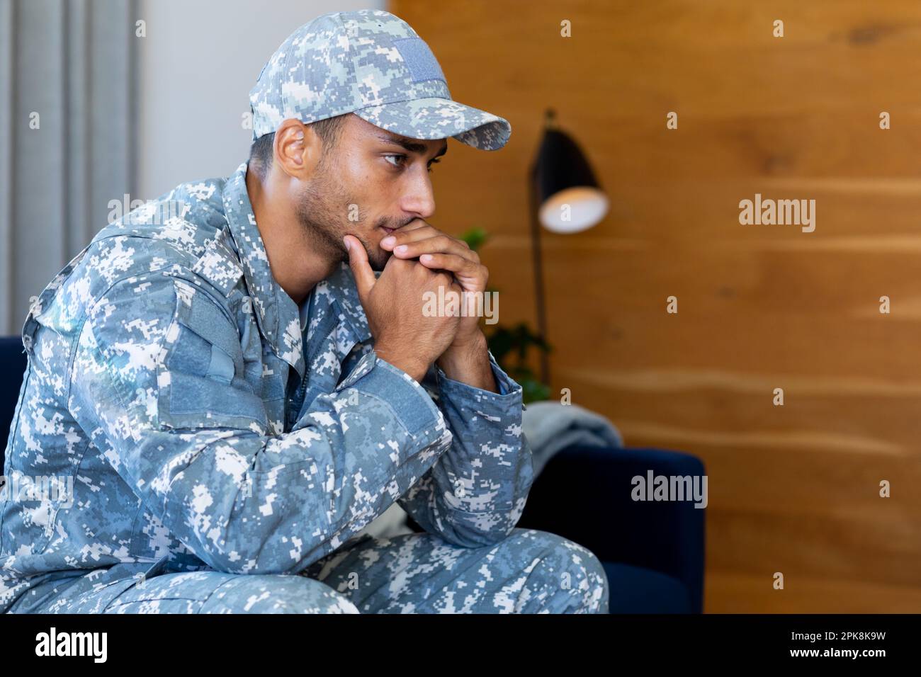 Thoughtful biracial male soldier wearing uniform and cap, sitting on ...