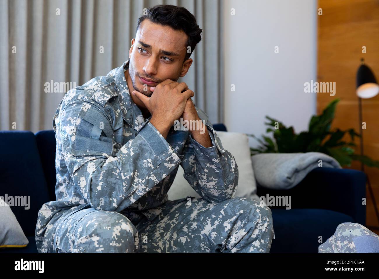 Thoughtful biracial male soldier wearing military uniform, sitting on ...