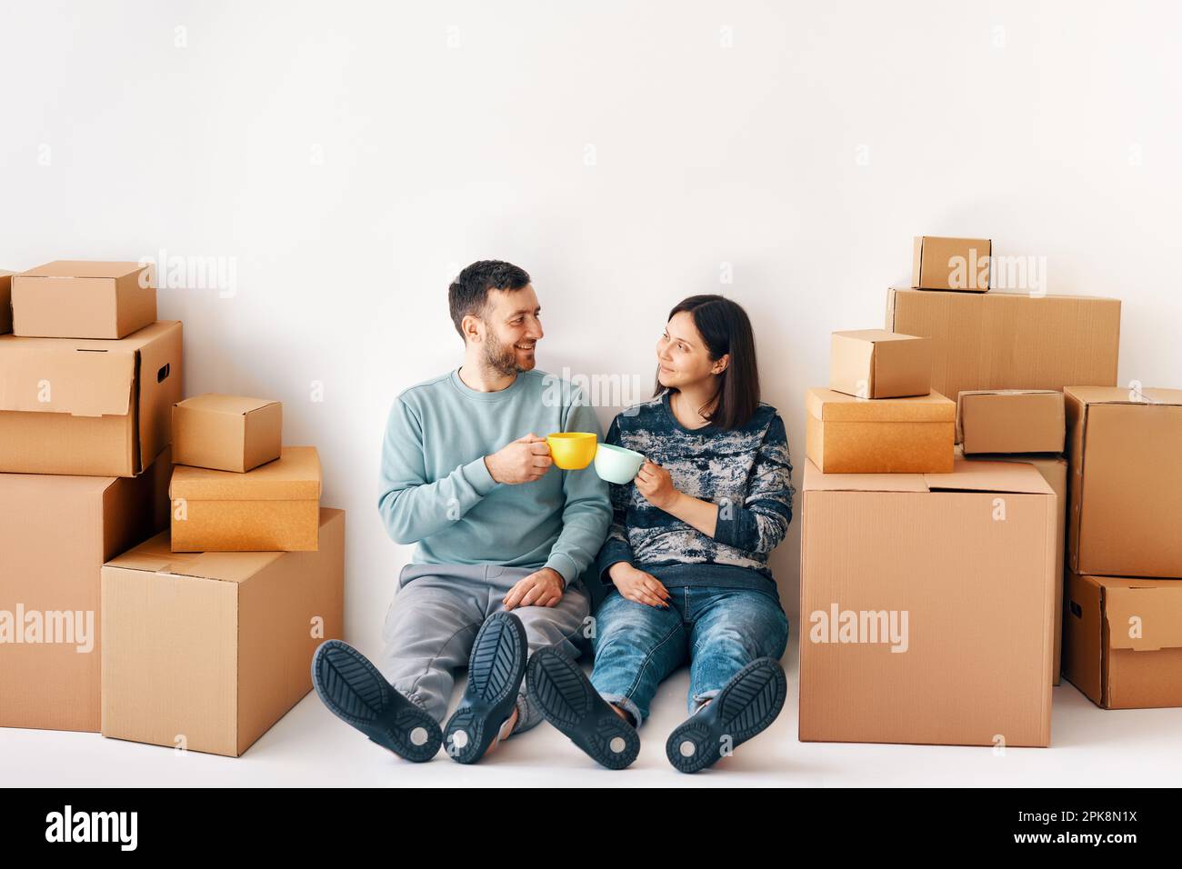 Young couple taking a break on moving day sitting on floor and ...