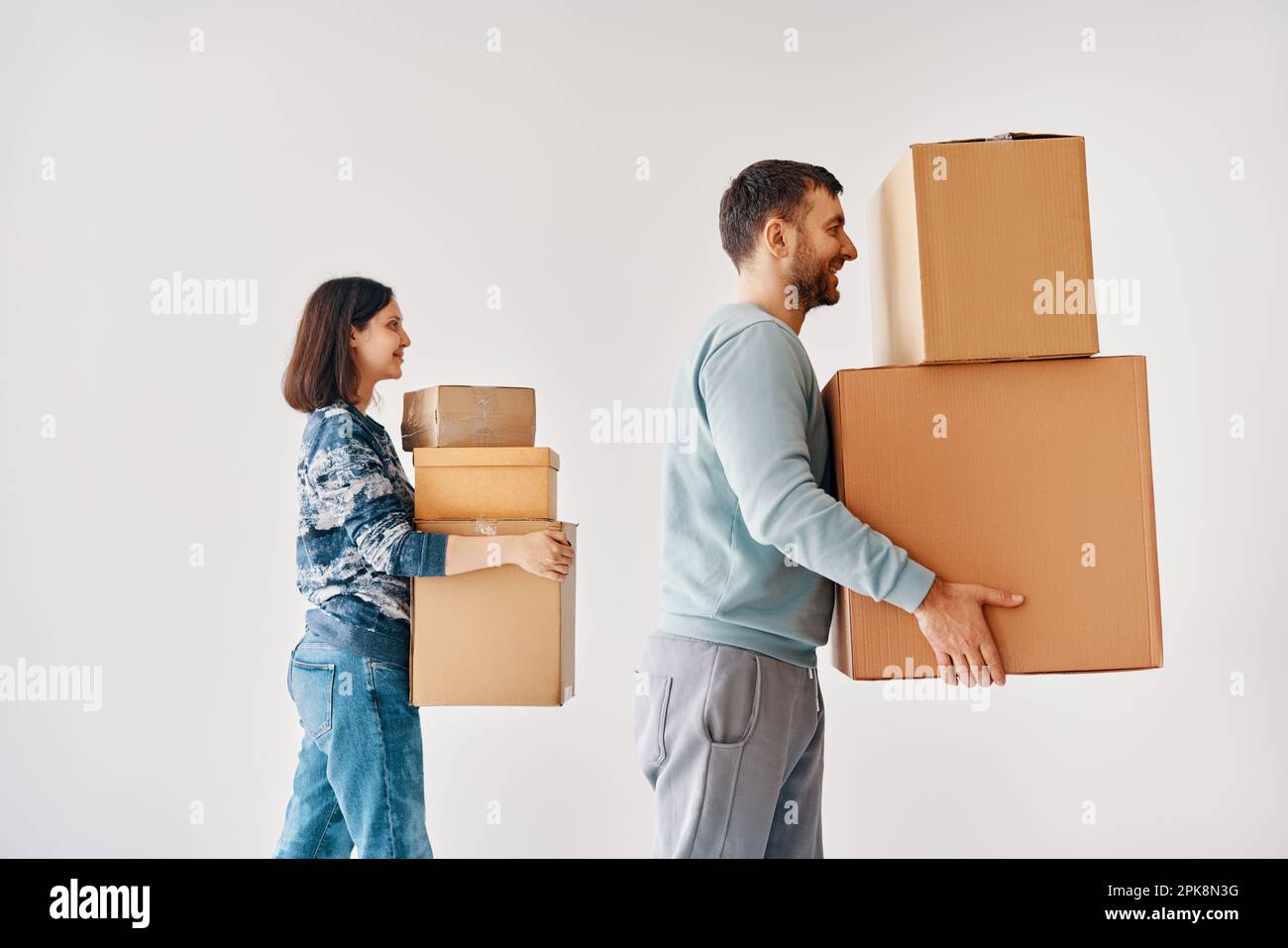 Profile view of young couple carrying cardboard boxes moving to new ...