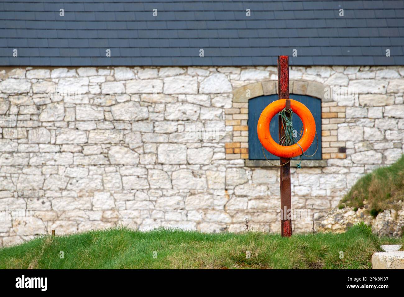 Orange lifesaver ring on a post in front of an old stone building Stock ...