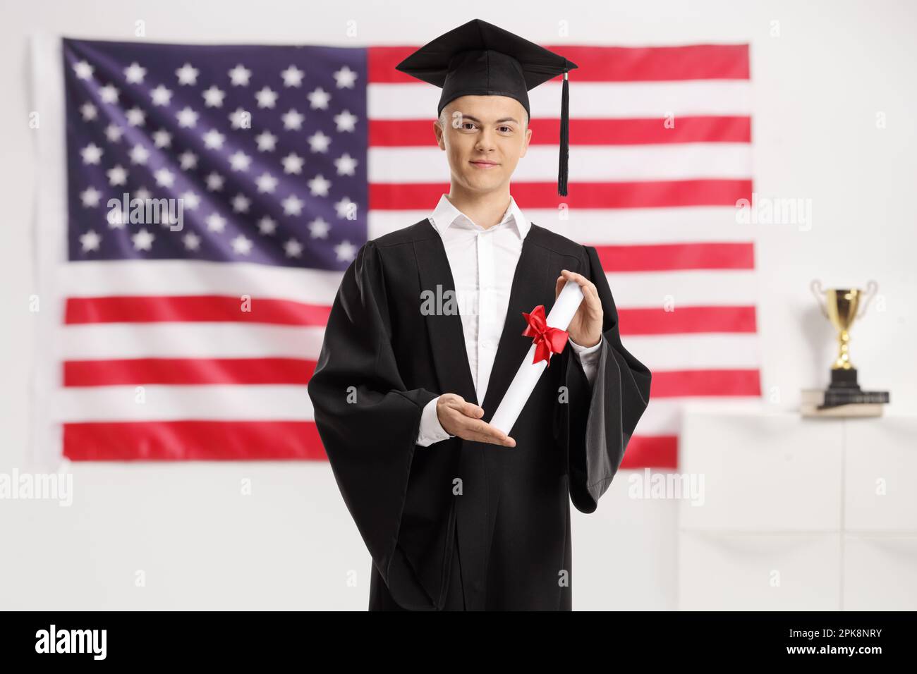 Graduate male student in a gown holding a diploma and standing in front ...
