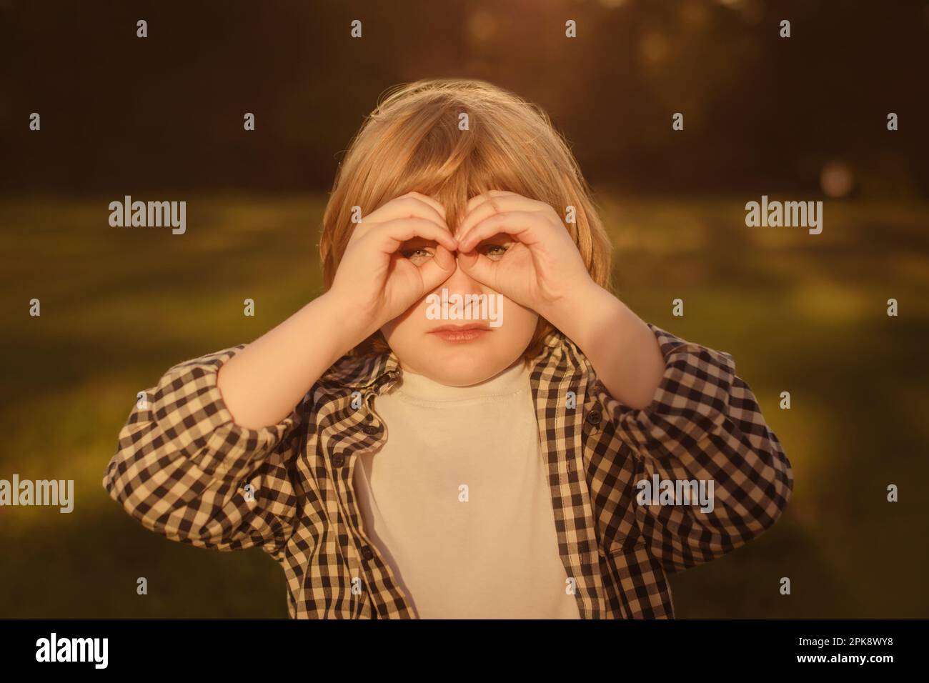 child boy in casual white t-shirt looking through fingers in binoculars ...