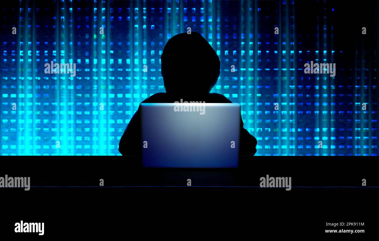 Dark person with hood silhouetted against open laptop and digital ...