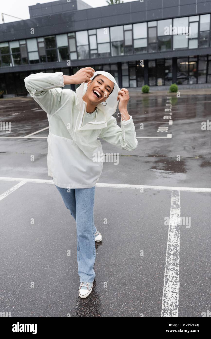 full length of excited african american woman in waterproof raincoat ...
