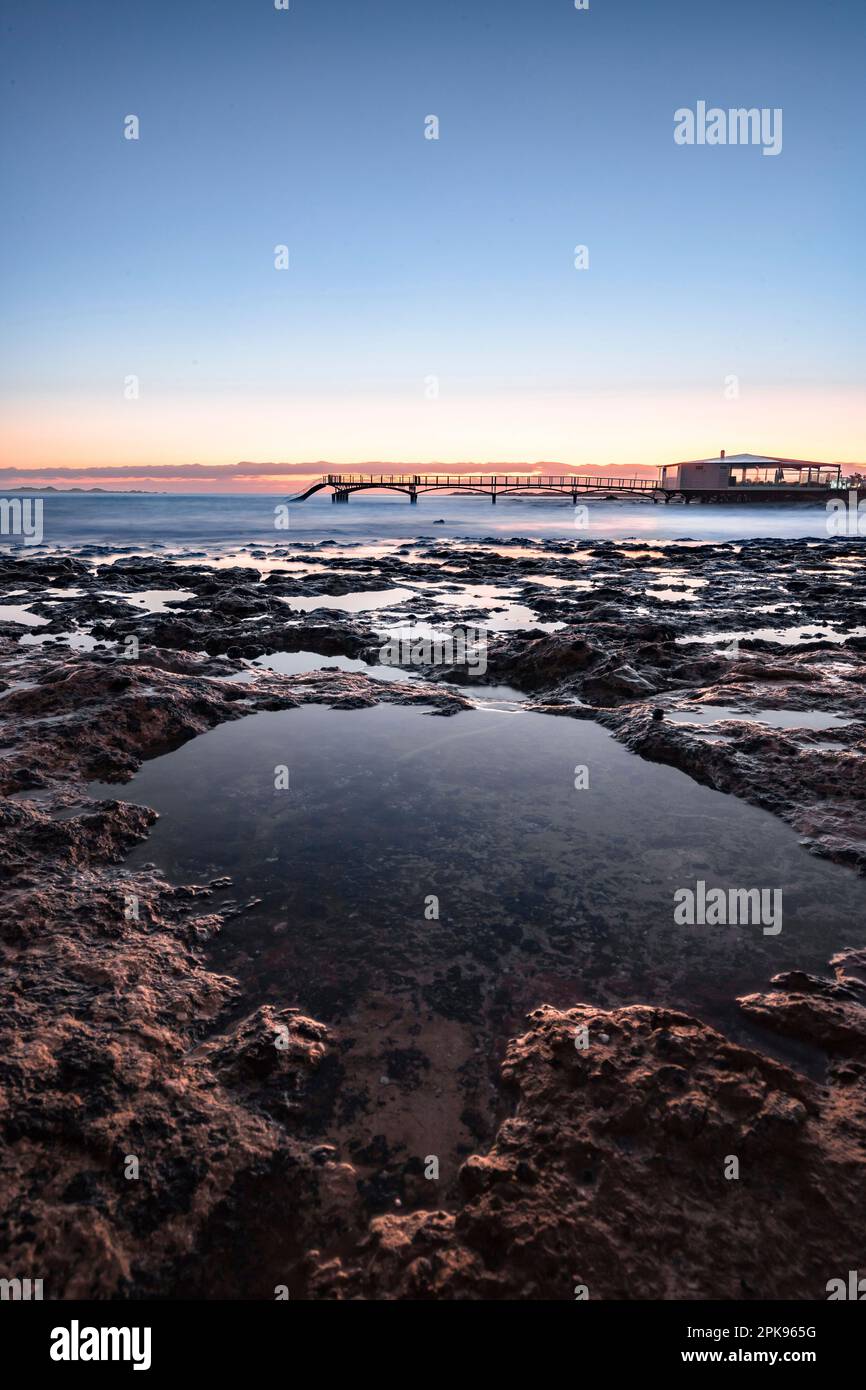 Sunrise on beach, lava rocks and sandy beach in long exposure. Romantic ...