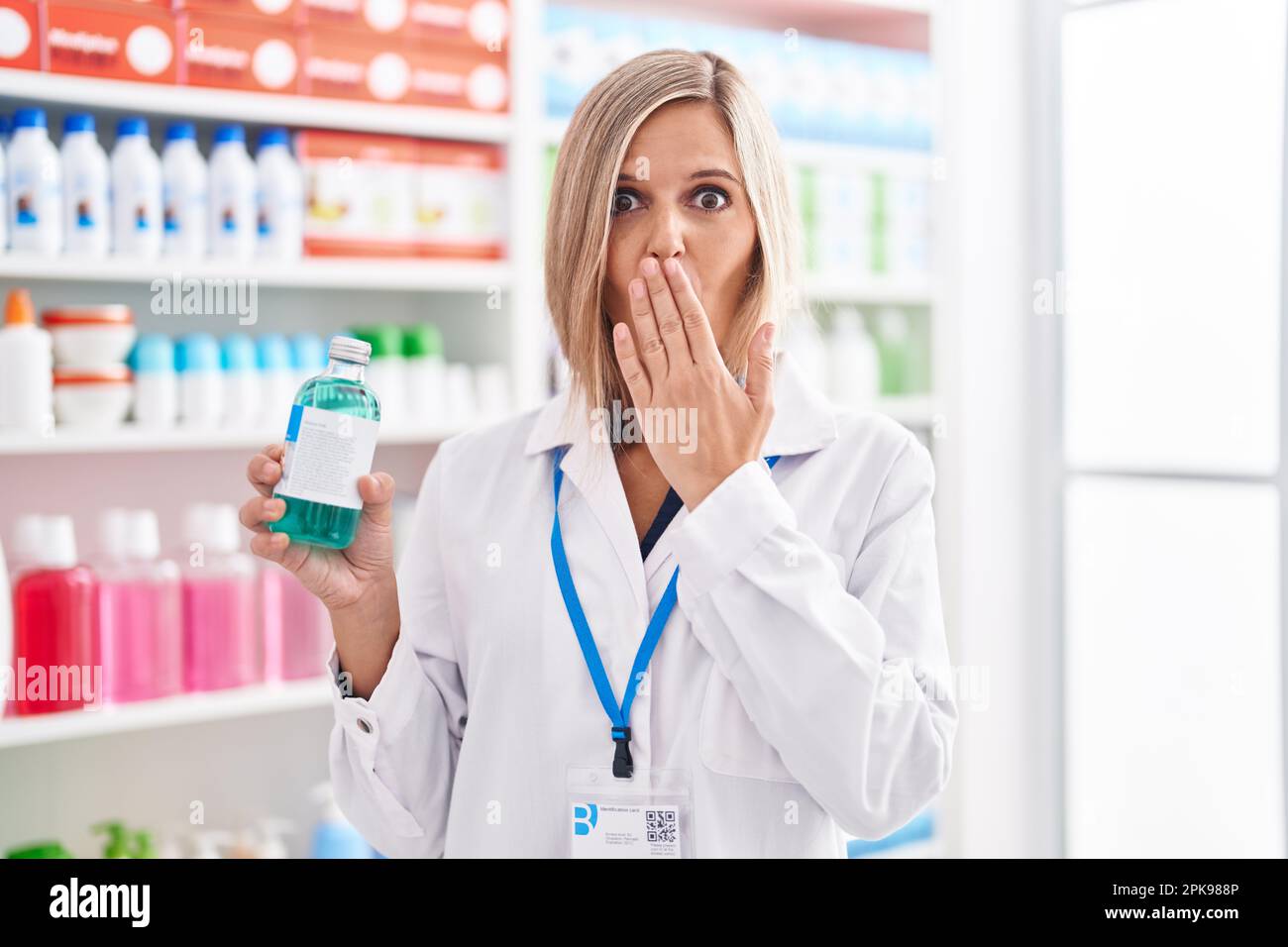 Blonde woman working at pharmacy drugstore holding syrup covering mouth ...