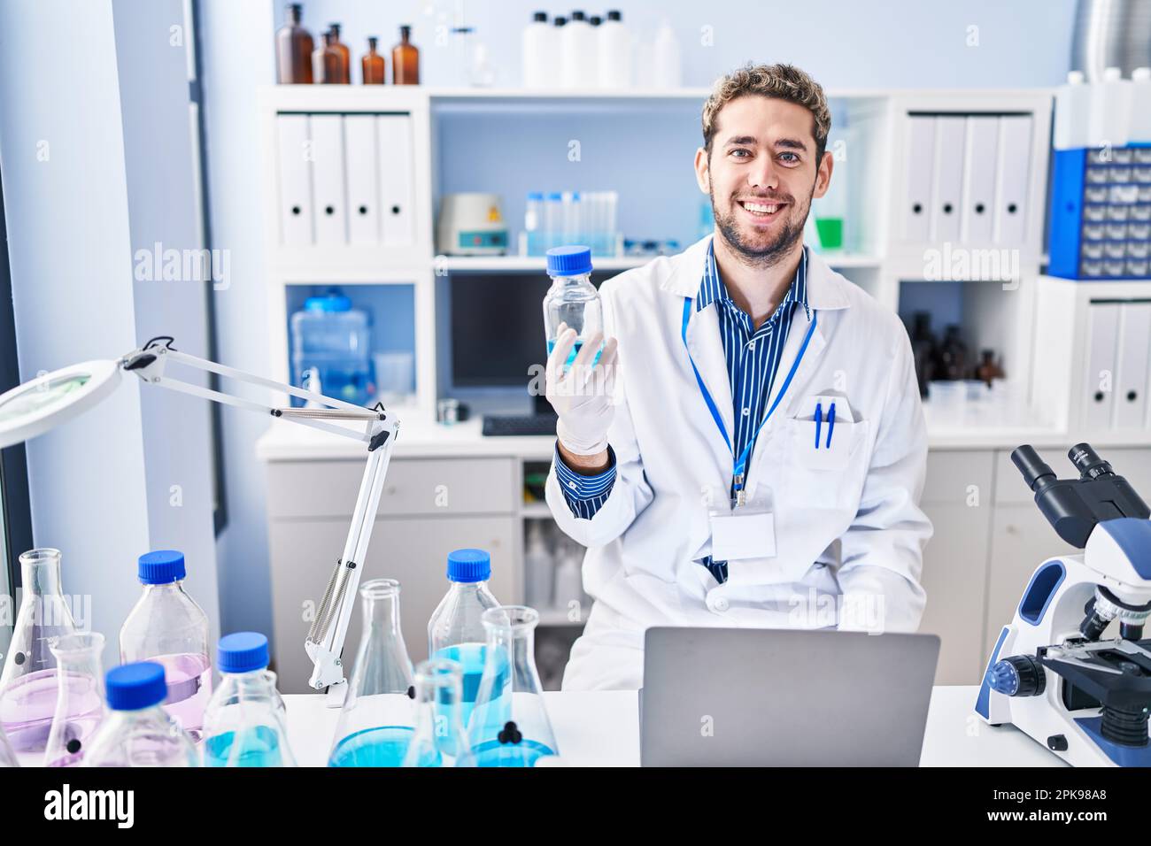 Young man scientist using laptop holding bottle at laboratory Stock ...