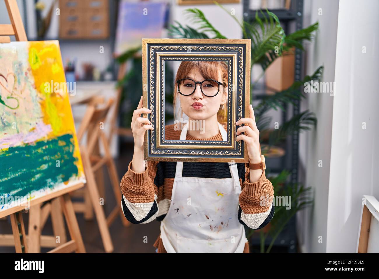 Young beautiful artist woman with face inside empty vintage frame ...