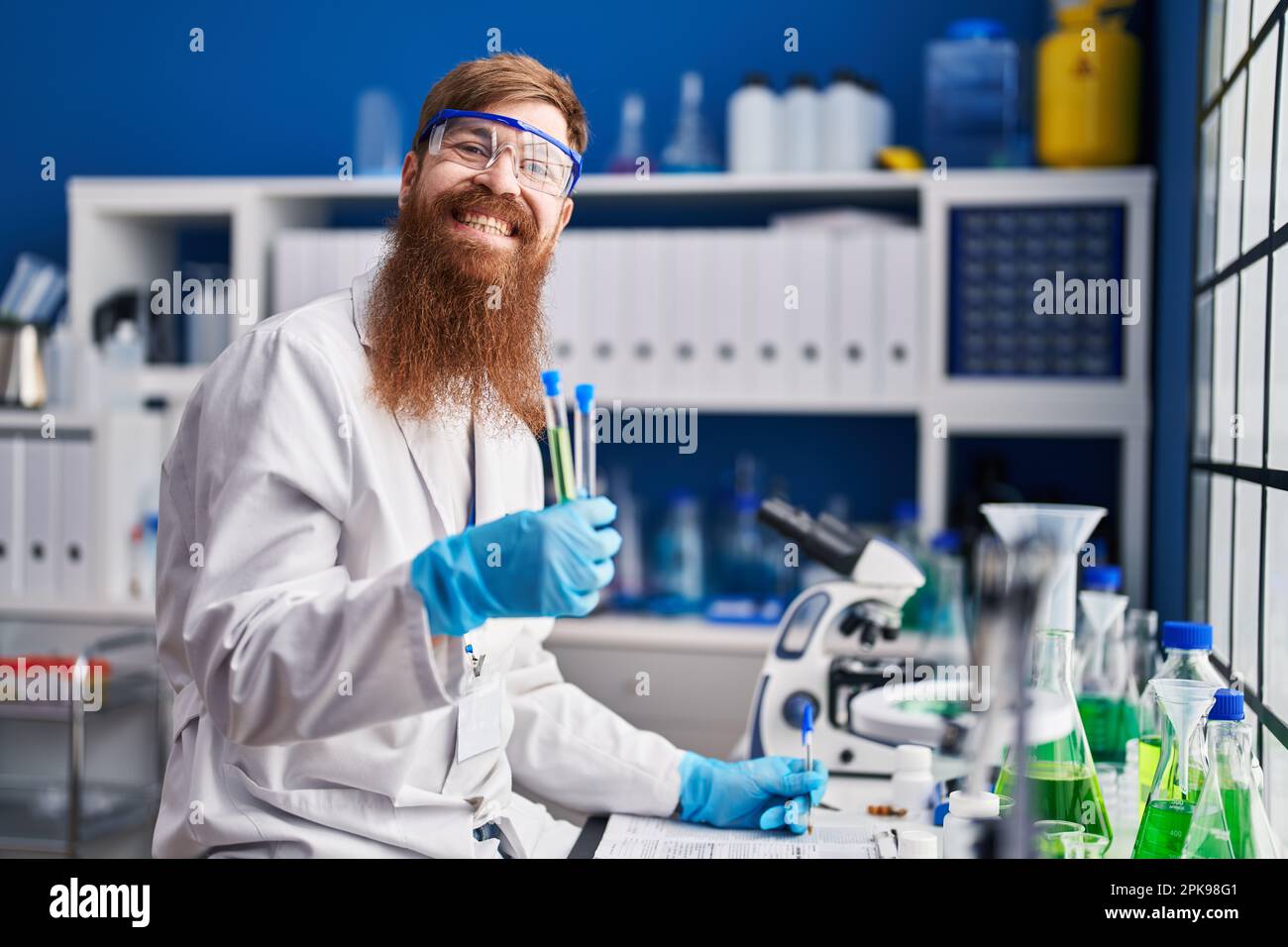 Young redhead man scientist holding test tubes writing report working ...