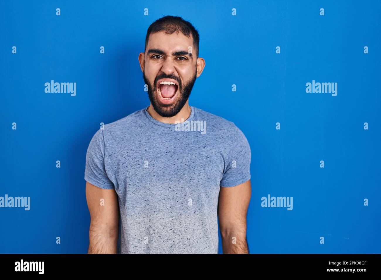 Middle east man with beard standing over blue background angry and mad ...