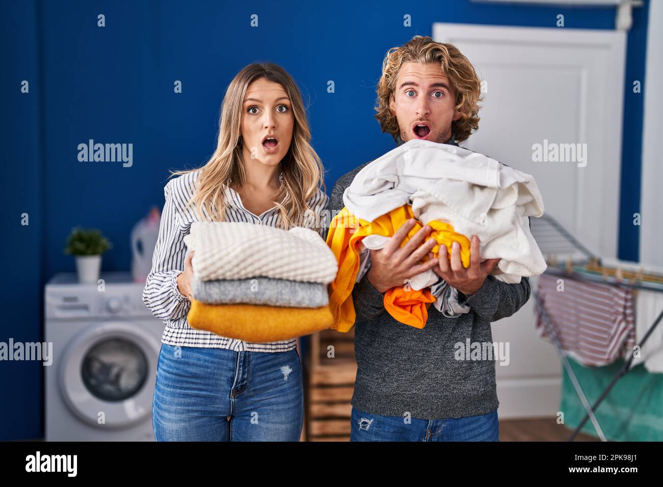 Young couple doing laundry in shock face, looking skeptical and ...
