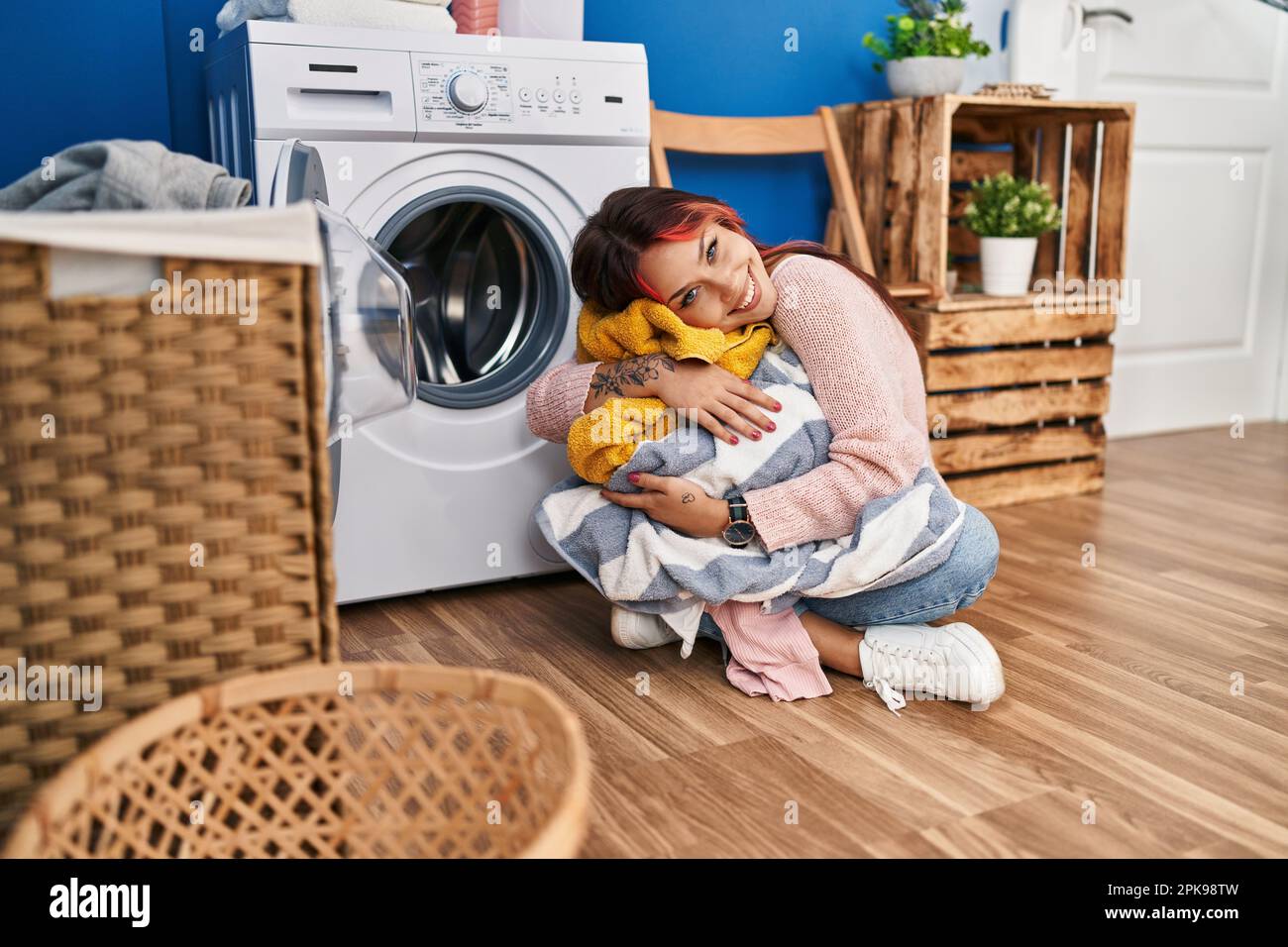 Young caucasian woman hugging clothes sitting on floor at laundry room ...