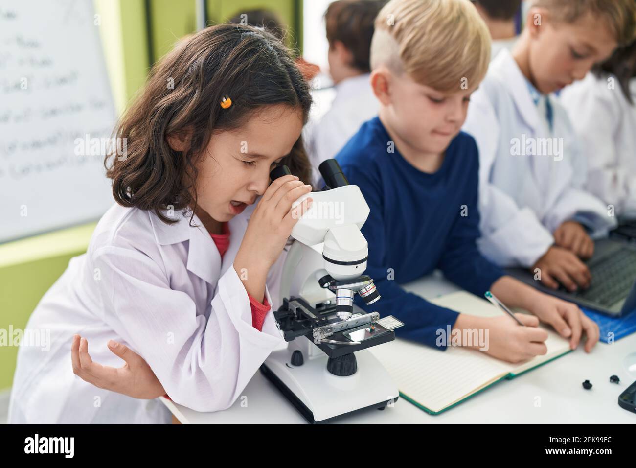 Group of kids students using microscope writing on notebook at ...