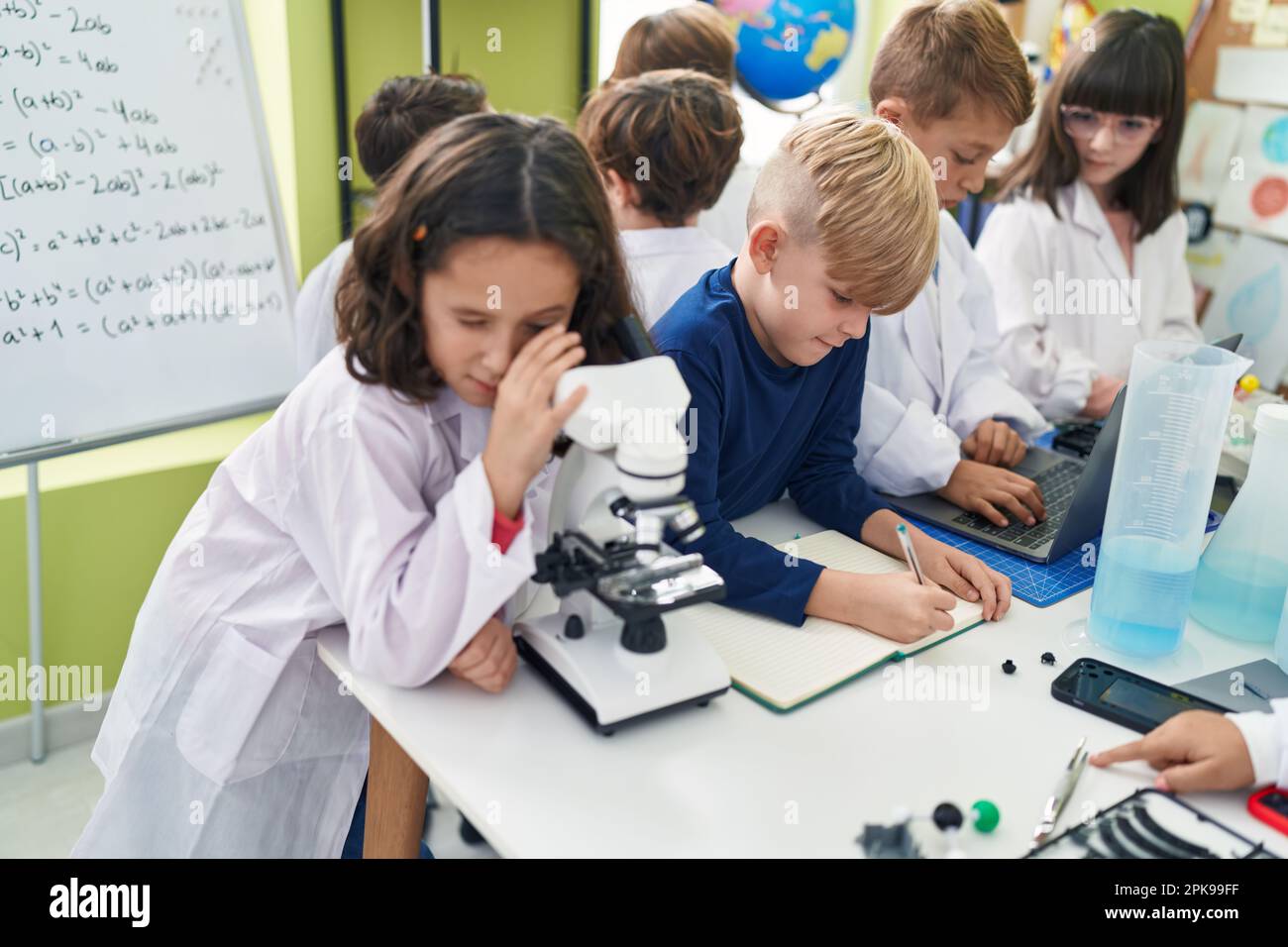 Group of kids students using microscope writing on notebook at ...