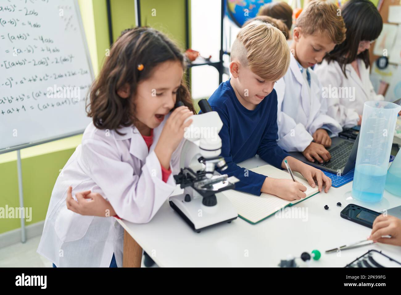 Group of kids students using microscope writing on notebook at ...