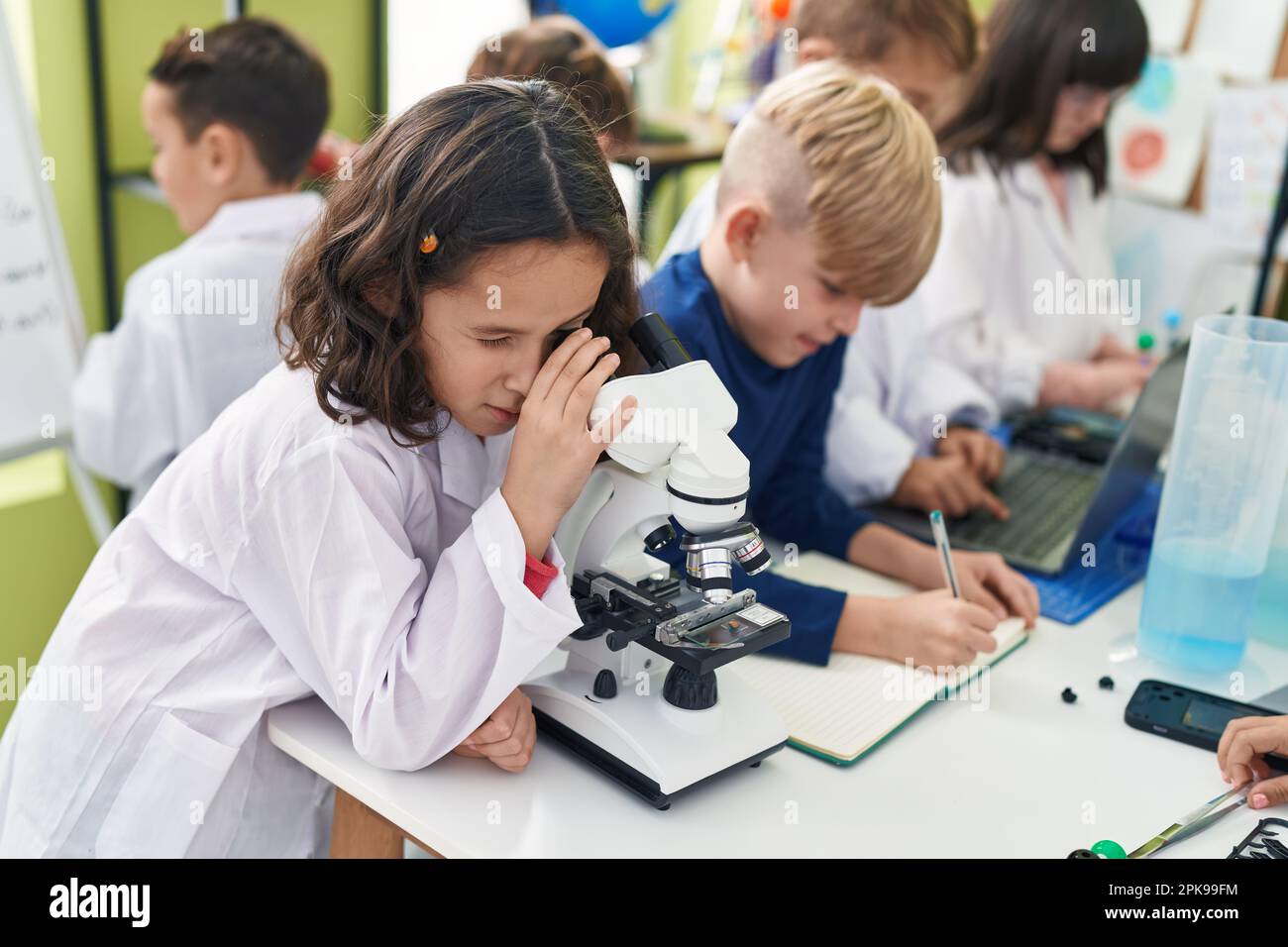 Group of kids students using microscope writing on notebook at ...
