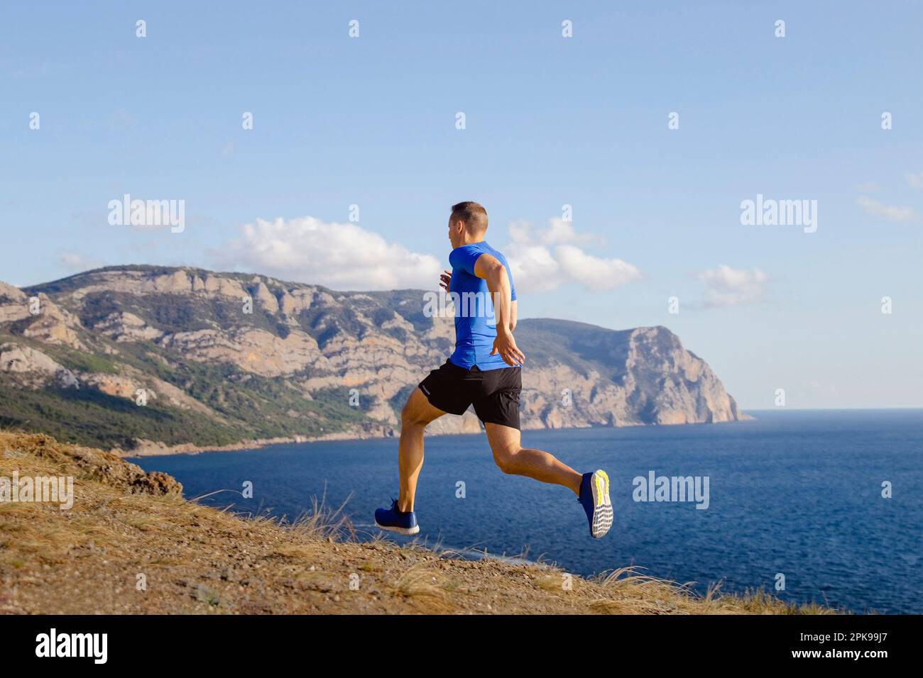 lean male runner run mountain trail along seashore, sports clothes blue ...