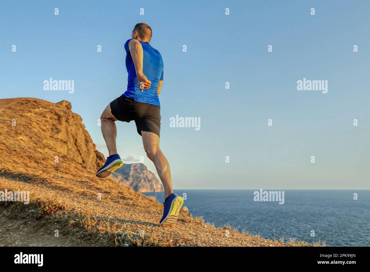 back male runner run uphill mountain trail in blue sky background ...