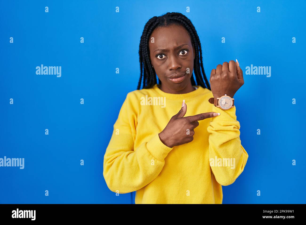 Beautiful black woman standing over blue background in hurry pointing ...