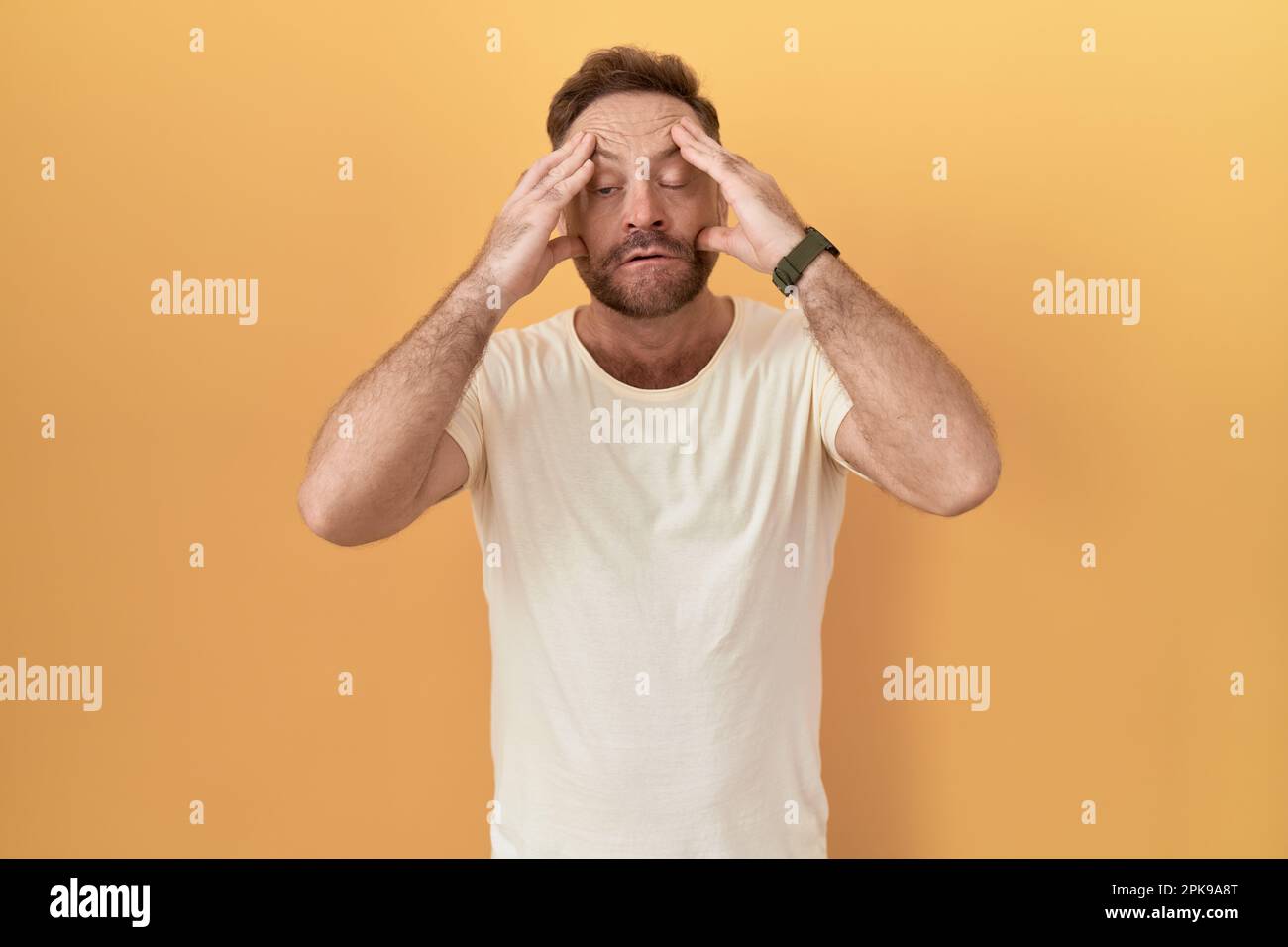 Middle age man with beard standing over yellow background trying to ...