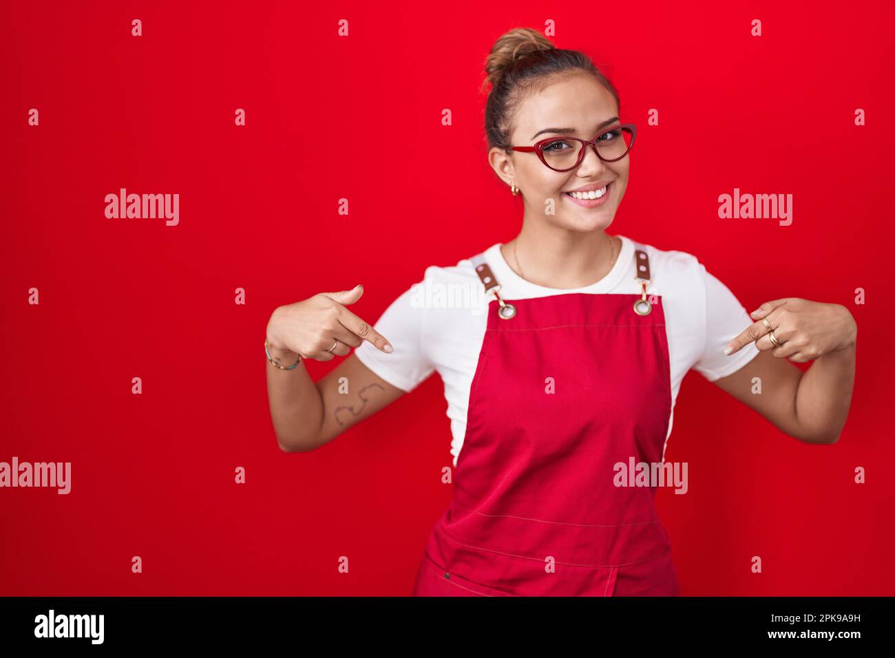 Young hispanic woman wearing waitress apron over red background looking ...