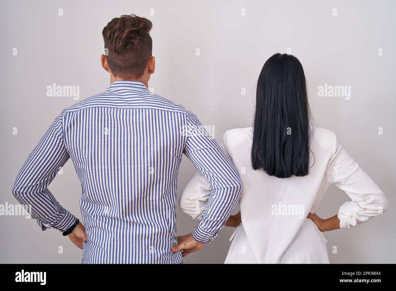 Young hispanic couple standing over white background standing backwards ...