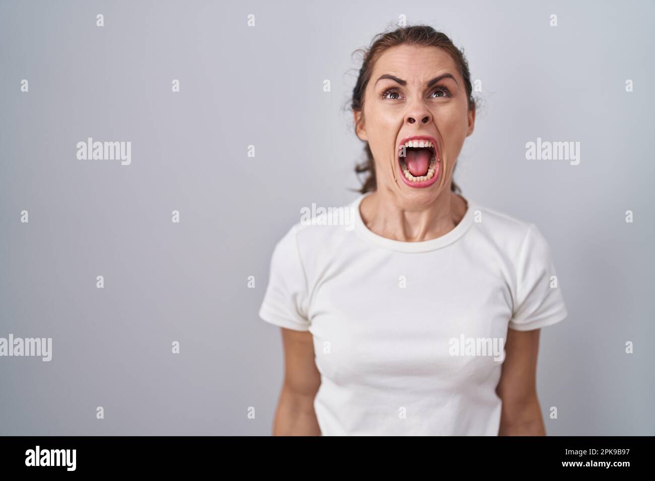 Beautiful brunette woman standing over isolated background angry and ...