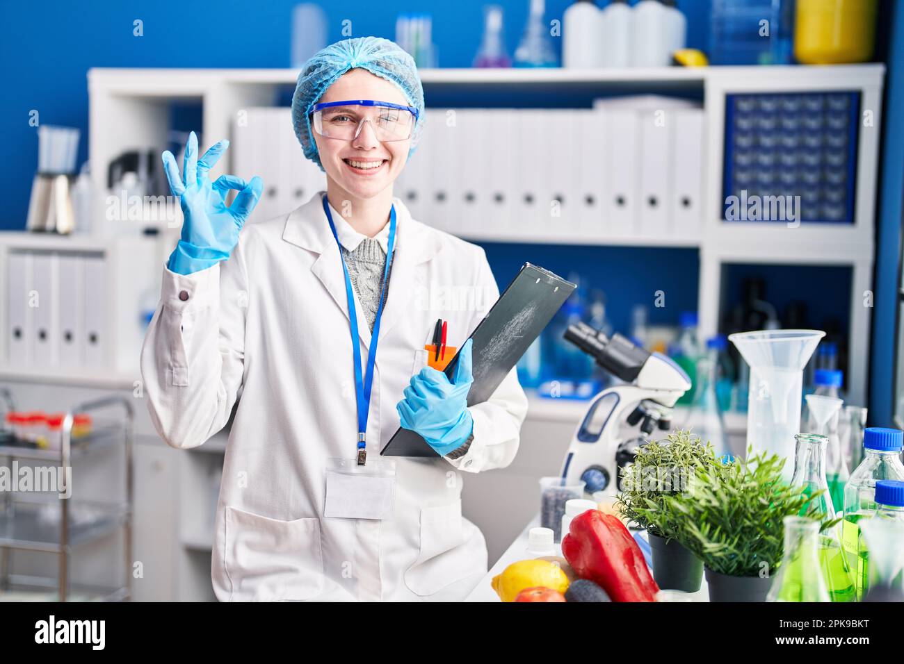 Beautiful woman working at scientist laboratory with food doing ok sign ...