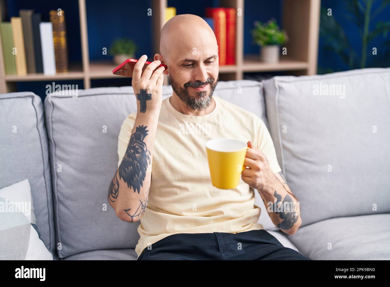 Young bald man listening voice message by smartphone drinking coffee at ...