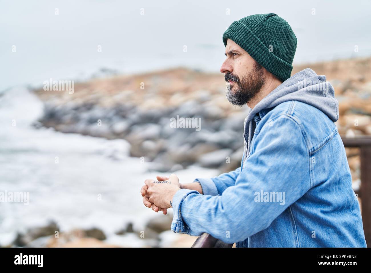 Young bald man leaning on balustrade with serious expression at seaside ...