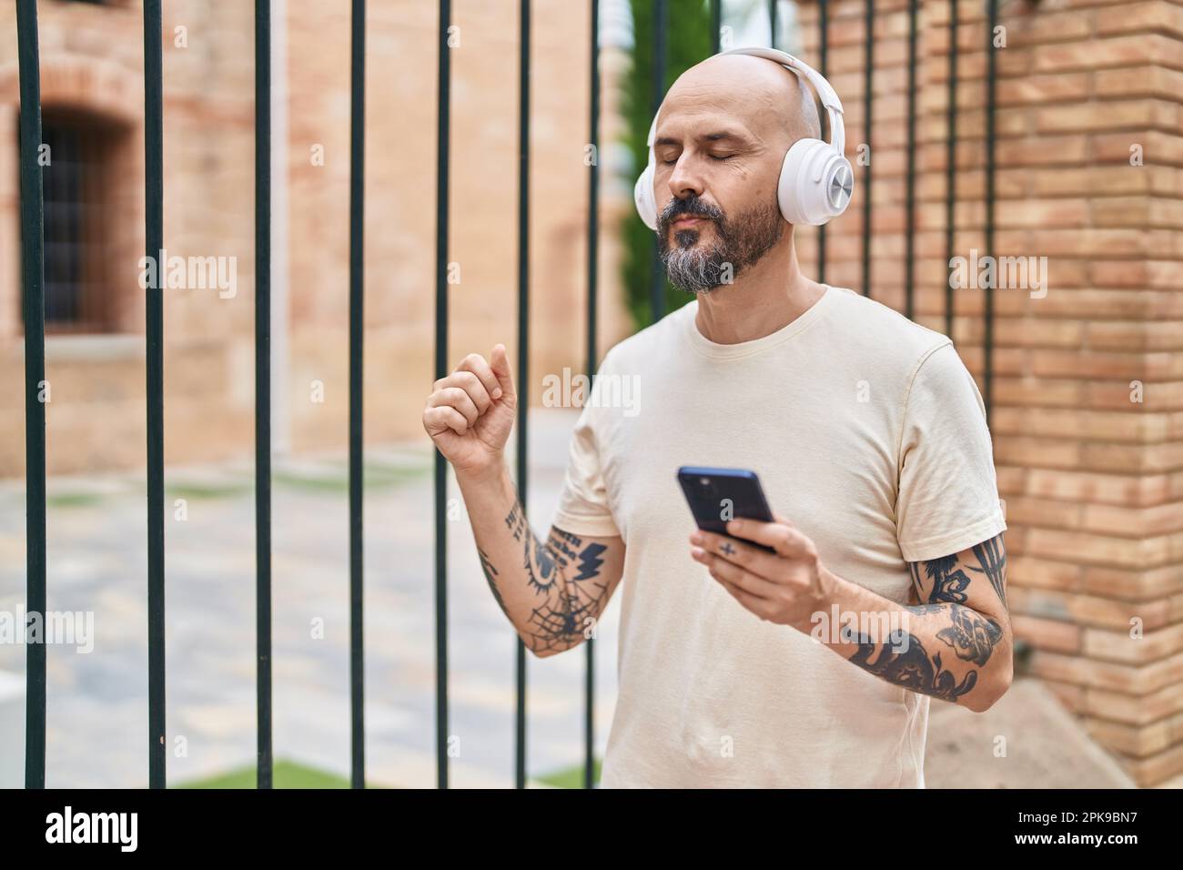 Young bald man listening to music and dancing with serious expression ...
