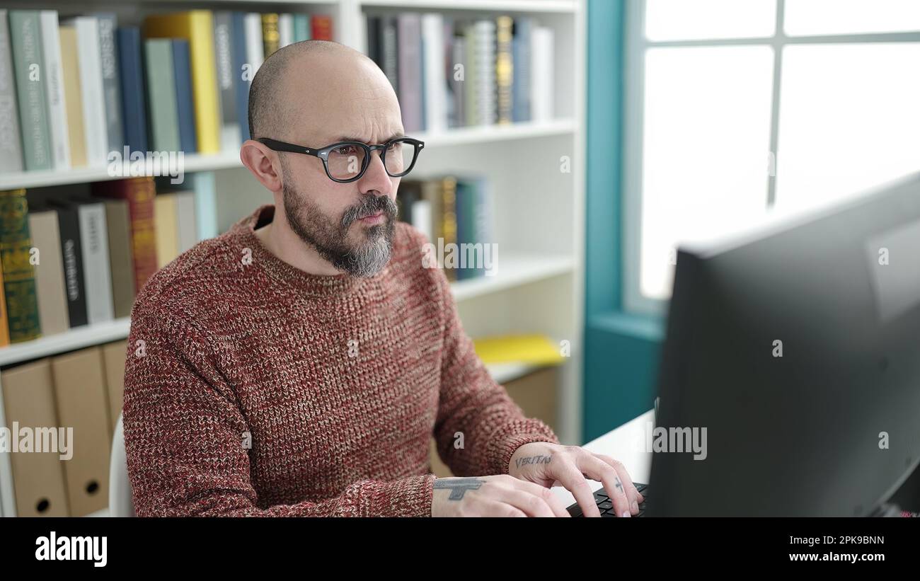 Young bald man student using computer studying at university classroom ...