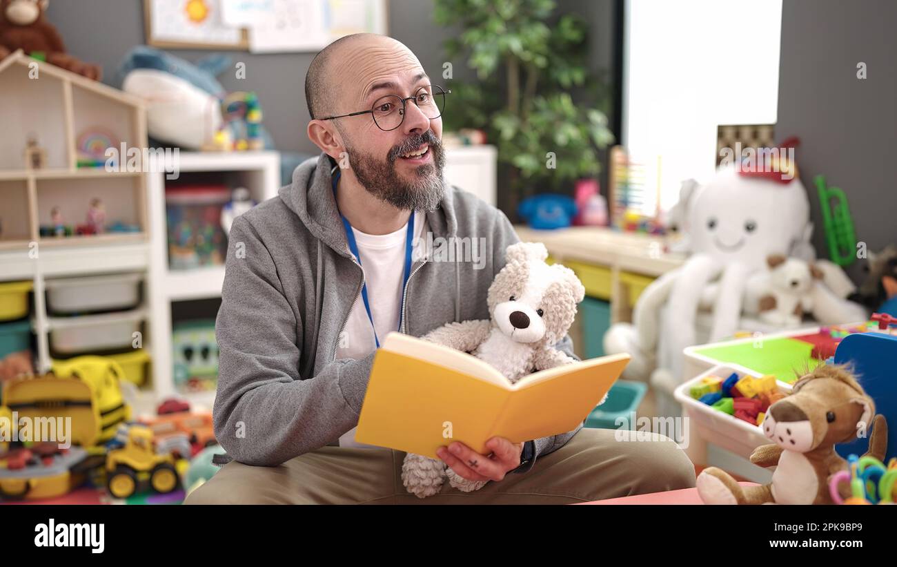 Young bald man preschool teacher reading story book at kindergarten ...