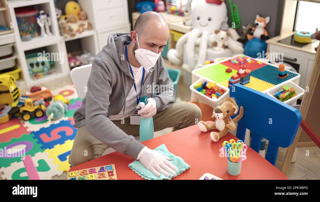 Young bald man preschool teacher wearing medical mask cleaning table at ...
