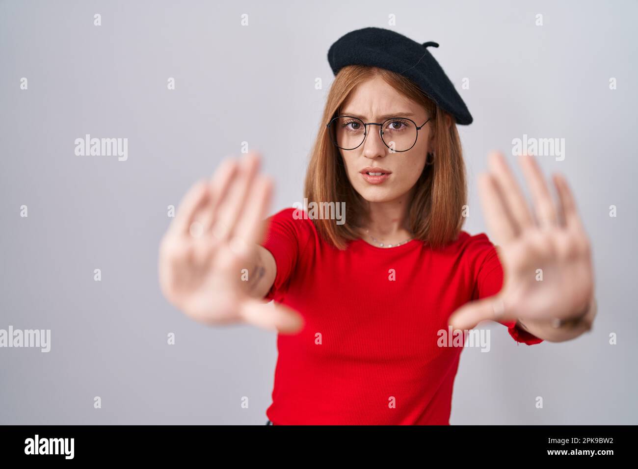 Young redhead woman standing wearing glasses and beret doing stop ...