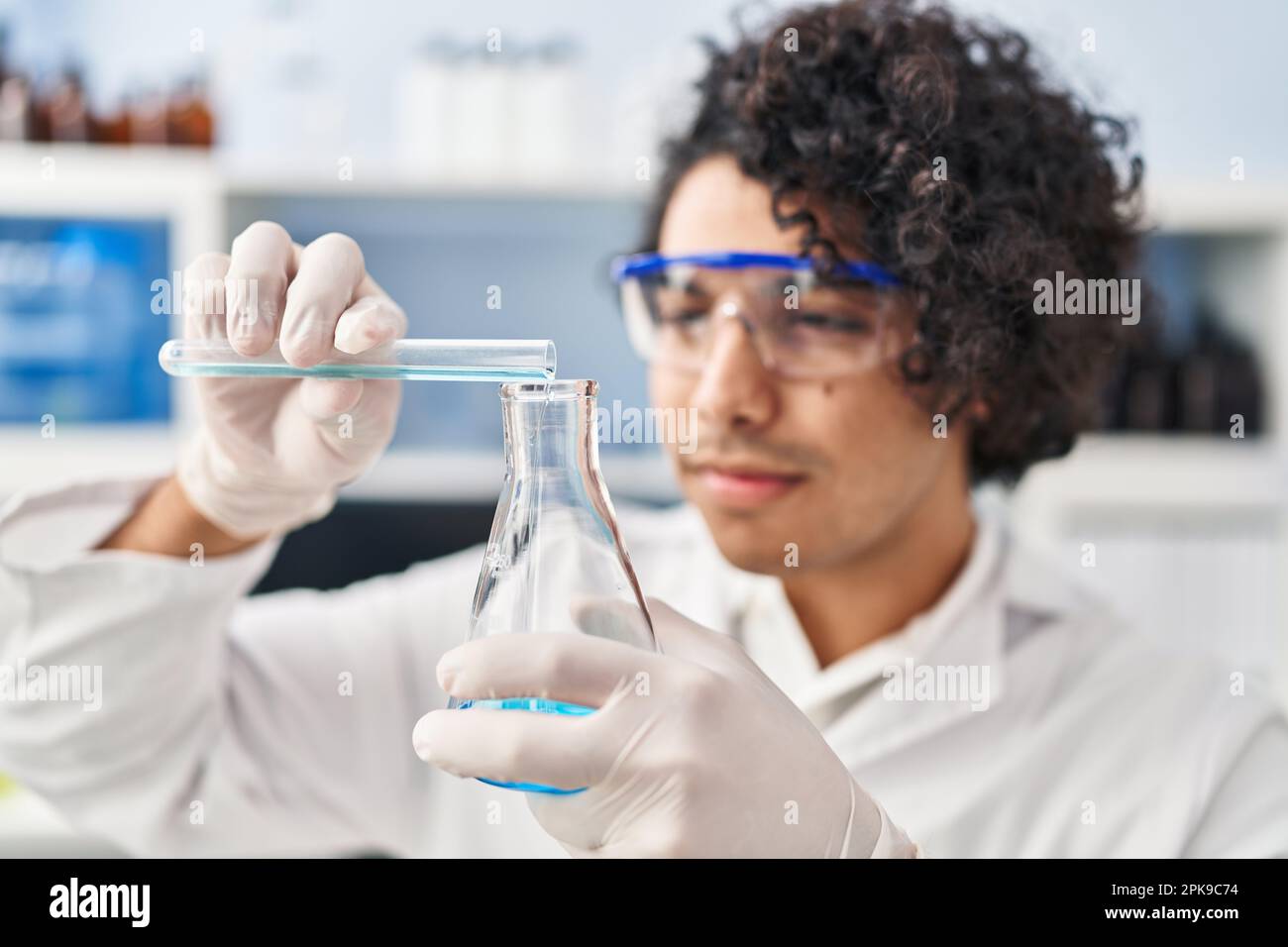 Young hispanic man wearing scientist uniform pouring liquid on test ...