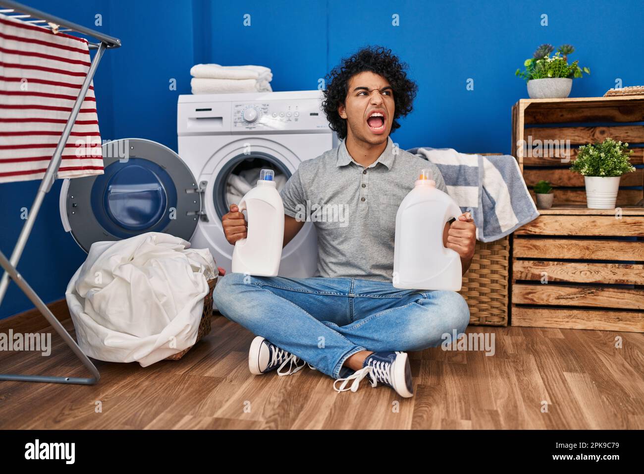 Hispanic man with curly hair doing laundry holding detergent bottles ...