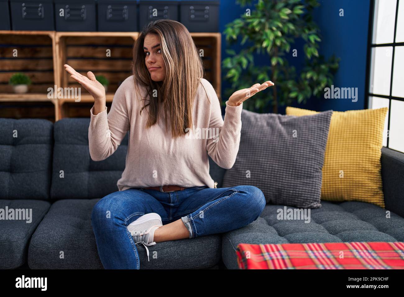 Beautiful woman sitting on the sofa at home clueless and confused ...
