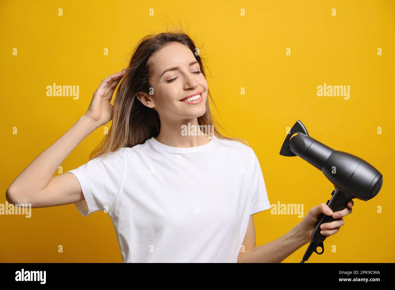 Beautiful young woman using hair dryer on yellow background Stock Photo ...