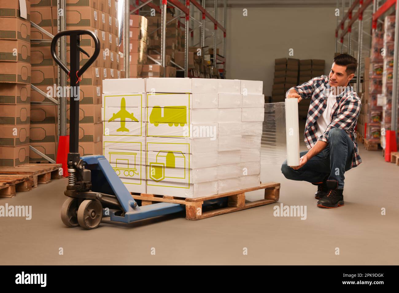 Worker wrapping boxes with shipping icons in stretch film at warehouse ...