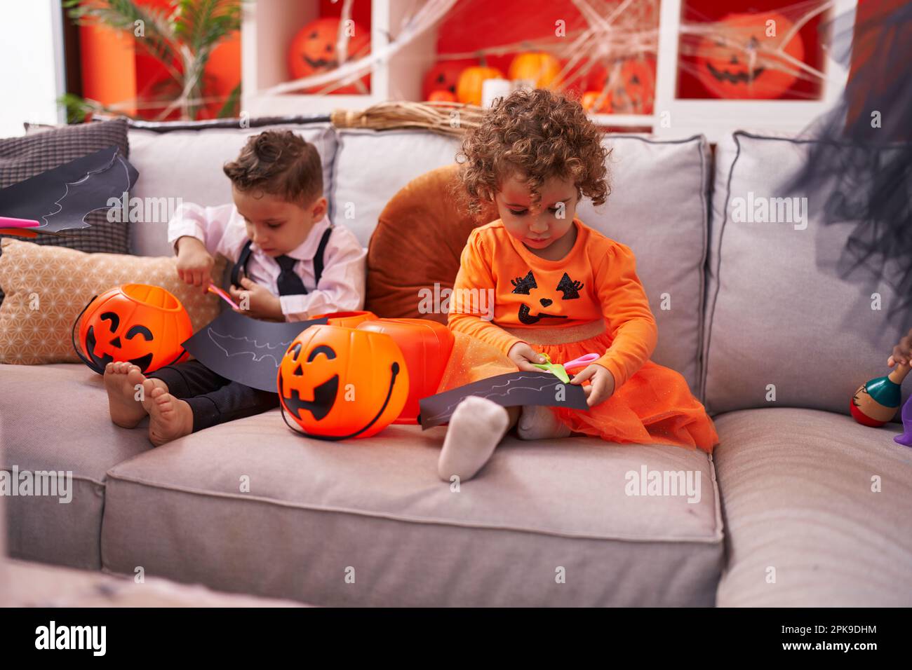 Adorable boy and girl having halloween party cutting paper at home ...