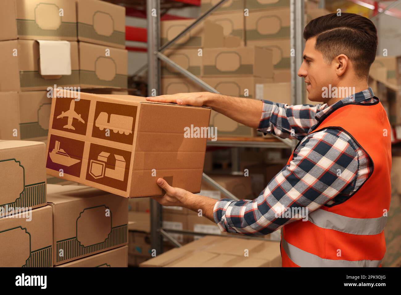Worker stacking cardboard boxes with shipping icons in warehouse ...