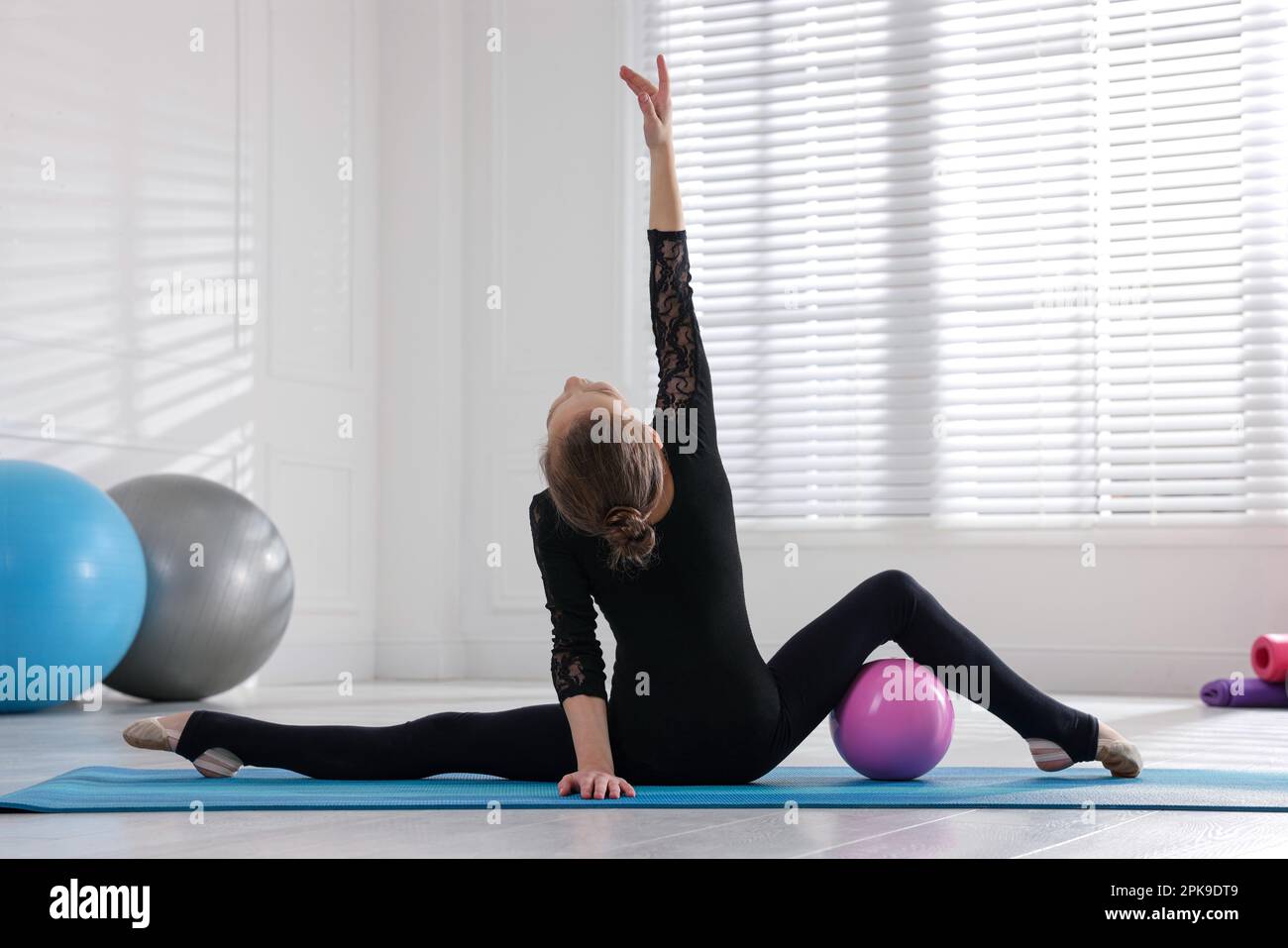 Cute little girl with ball doing gymnastics exercise indoors, back view ...