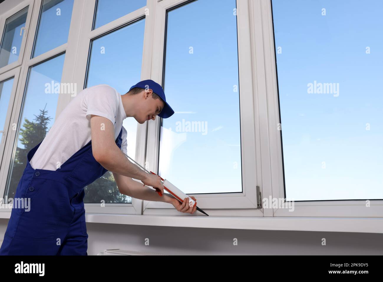 Worker sealing plastic window with caulk indoors. Installation process ...