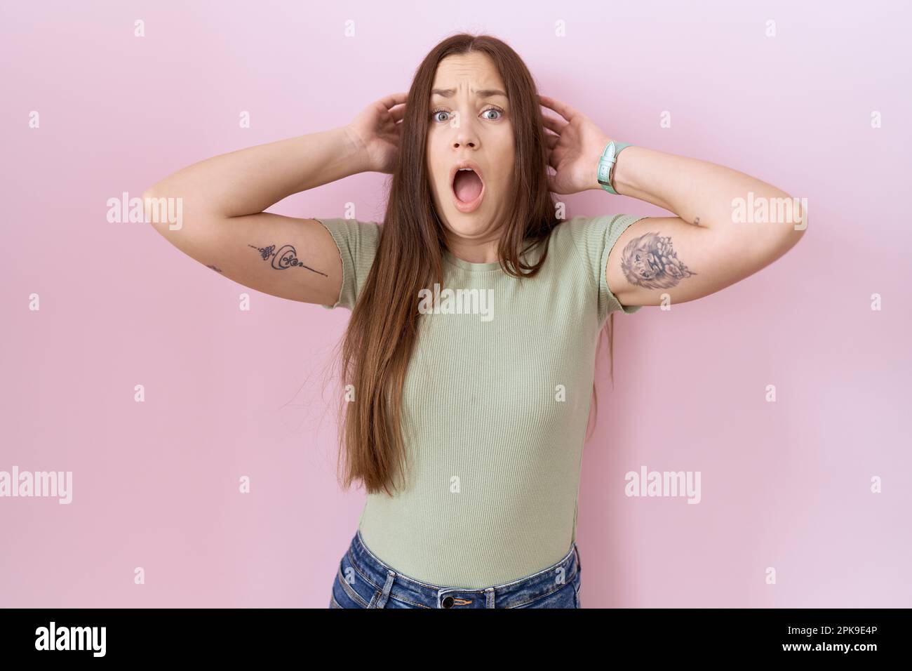 Beautiful brunette woman standing over pink background crazy and scared ...