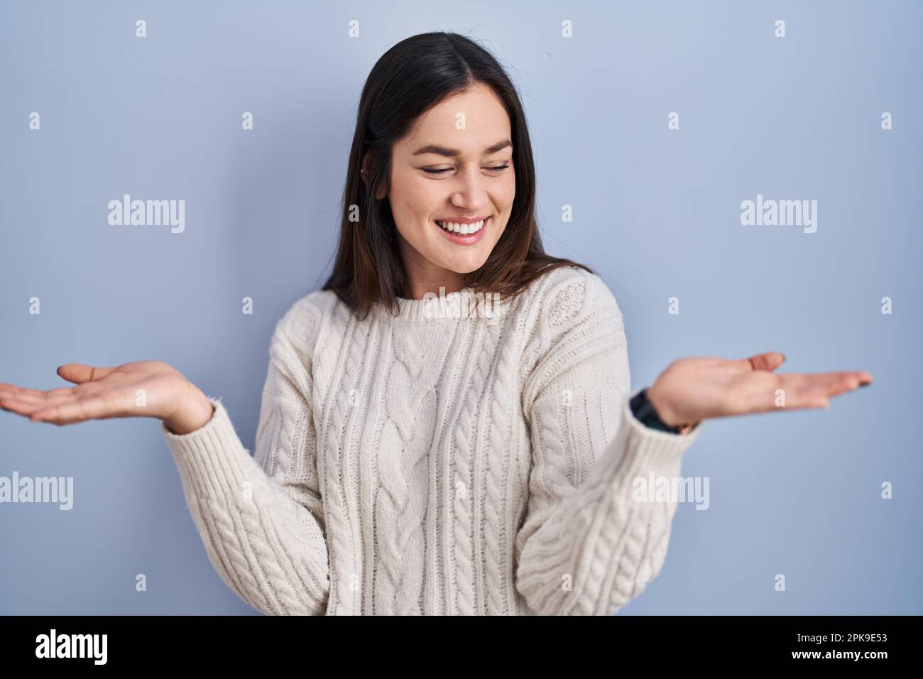 Young brunette woman standing over blue background smiling showing both ...