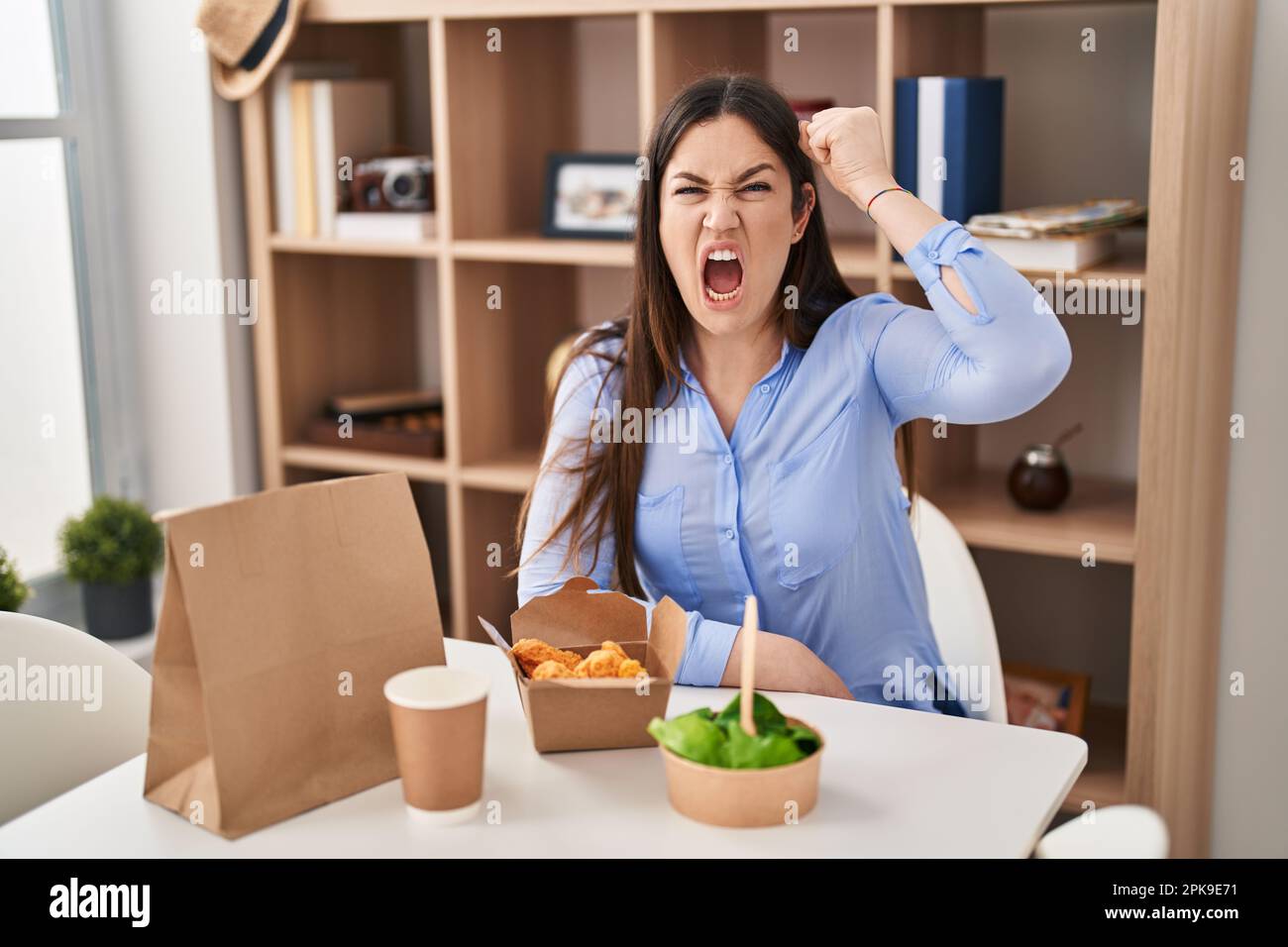 Young brunette woman eating take away food at home annoyed and ...